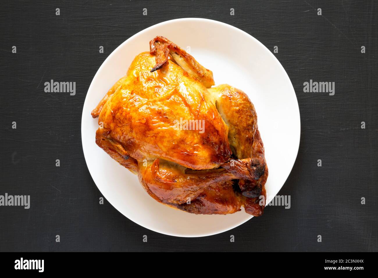 Homemade traditional rotisserie chicken on a white plate on a black ...