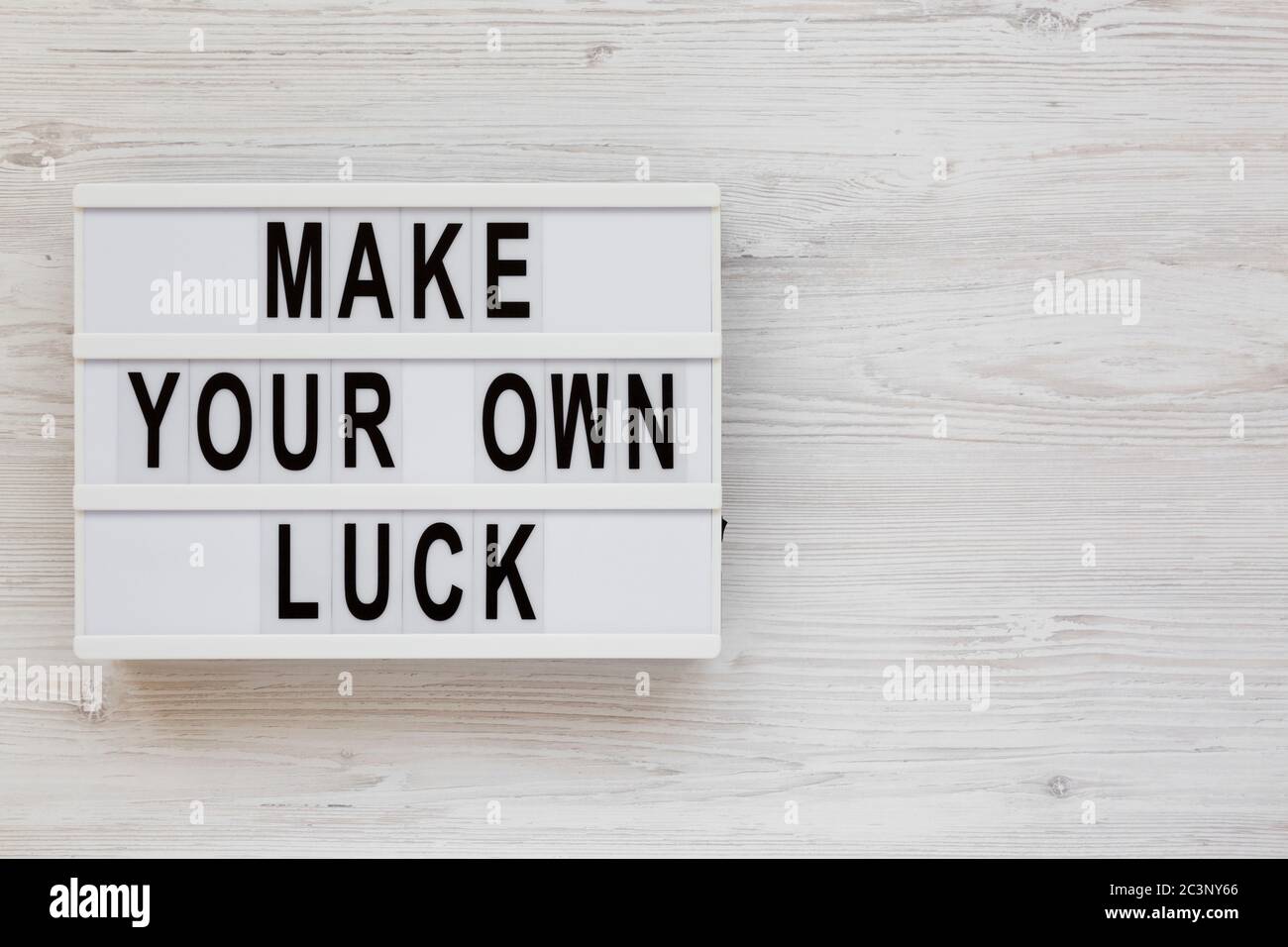 'Make your own luck' on a lightbox on a white wooden surface, top view ...