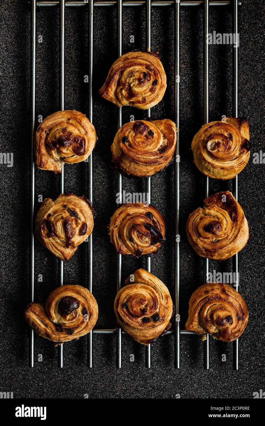 Puff pastry snails with custard and raisins cooling down on a steel ...