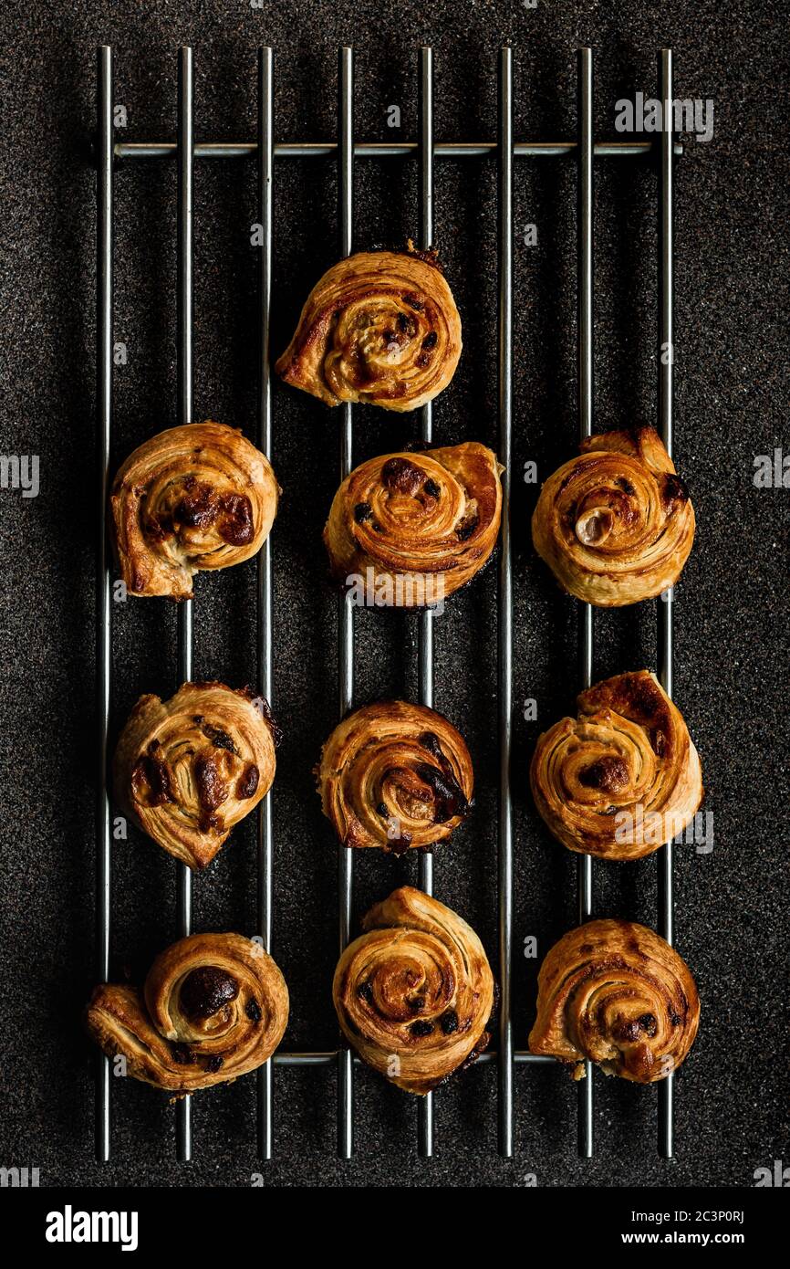 Puff pastry snails with custard and raisins cooling down on a steel ...