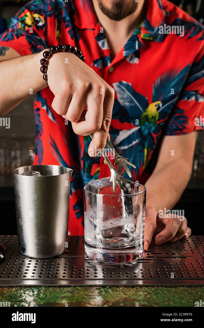 Bartender putting a crystal clear ice cube into a rocks glass. Tiki ...
