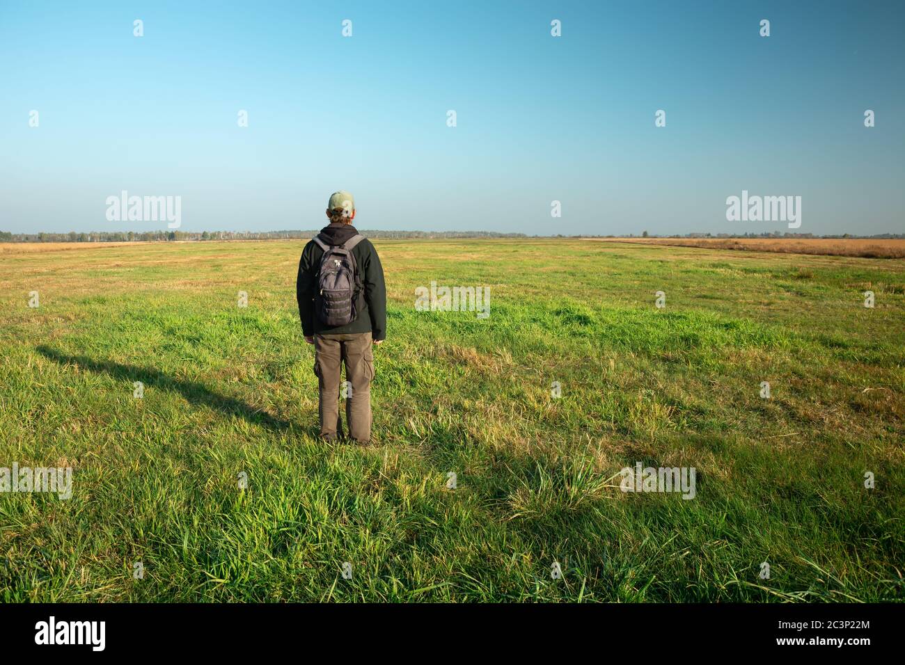A lone man with a backpack standing in front of a huge empty space ...