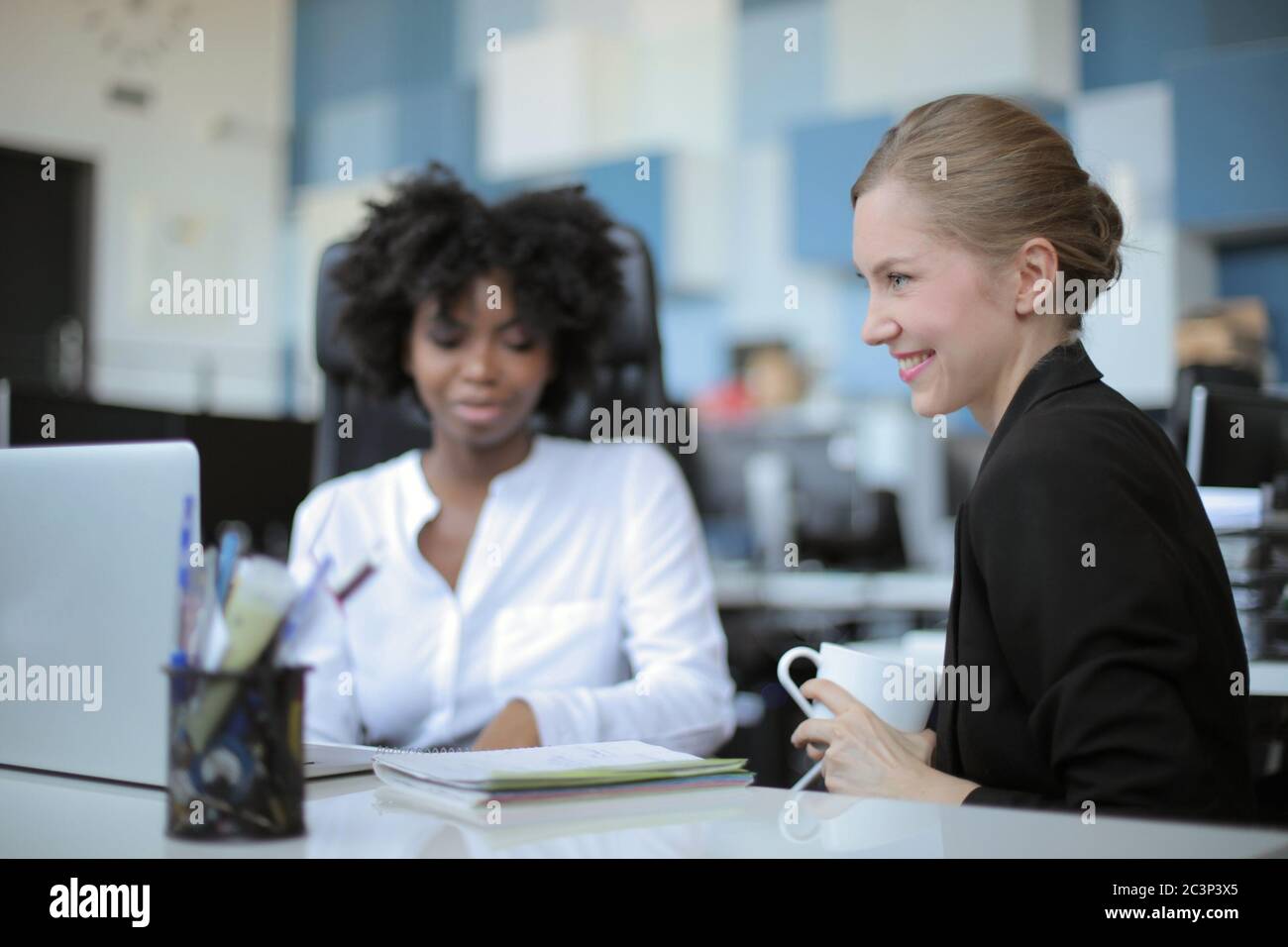 View of two female coworkers sitting side by side in an office-concept ...