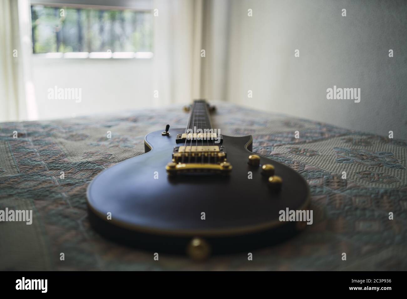 Closeup shot of a black electric guitar on a bed with patterned sheet ...