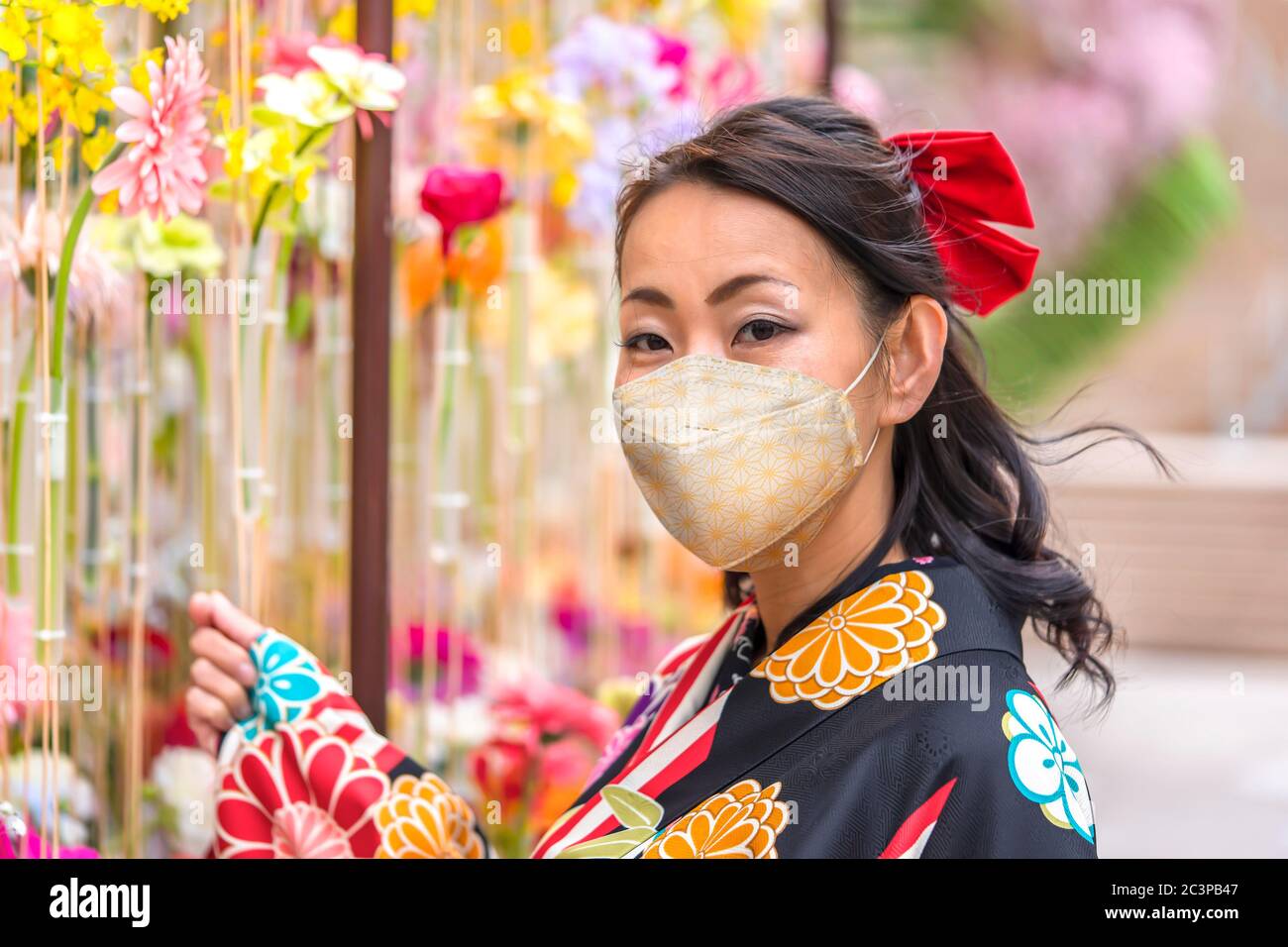 Japanese woman wearing a face mask in hakama kimono in front of a wall ...