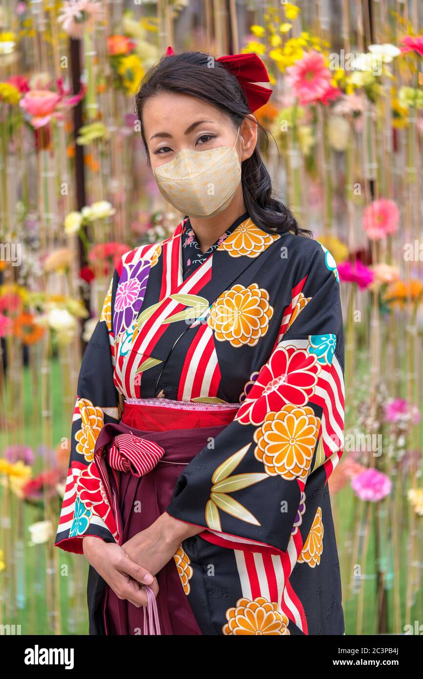 Japanese woman wearing a face mask in hakama kimono in front of a wall ...