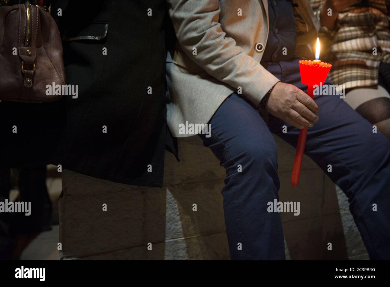 Man holding a burning red candle while seated Stock Photo - Alamy