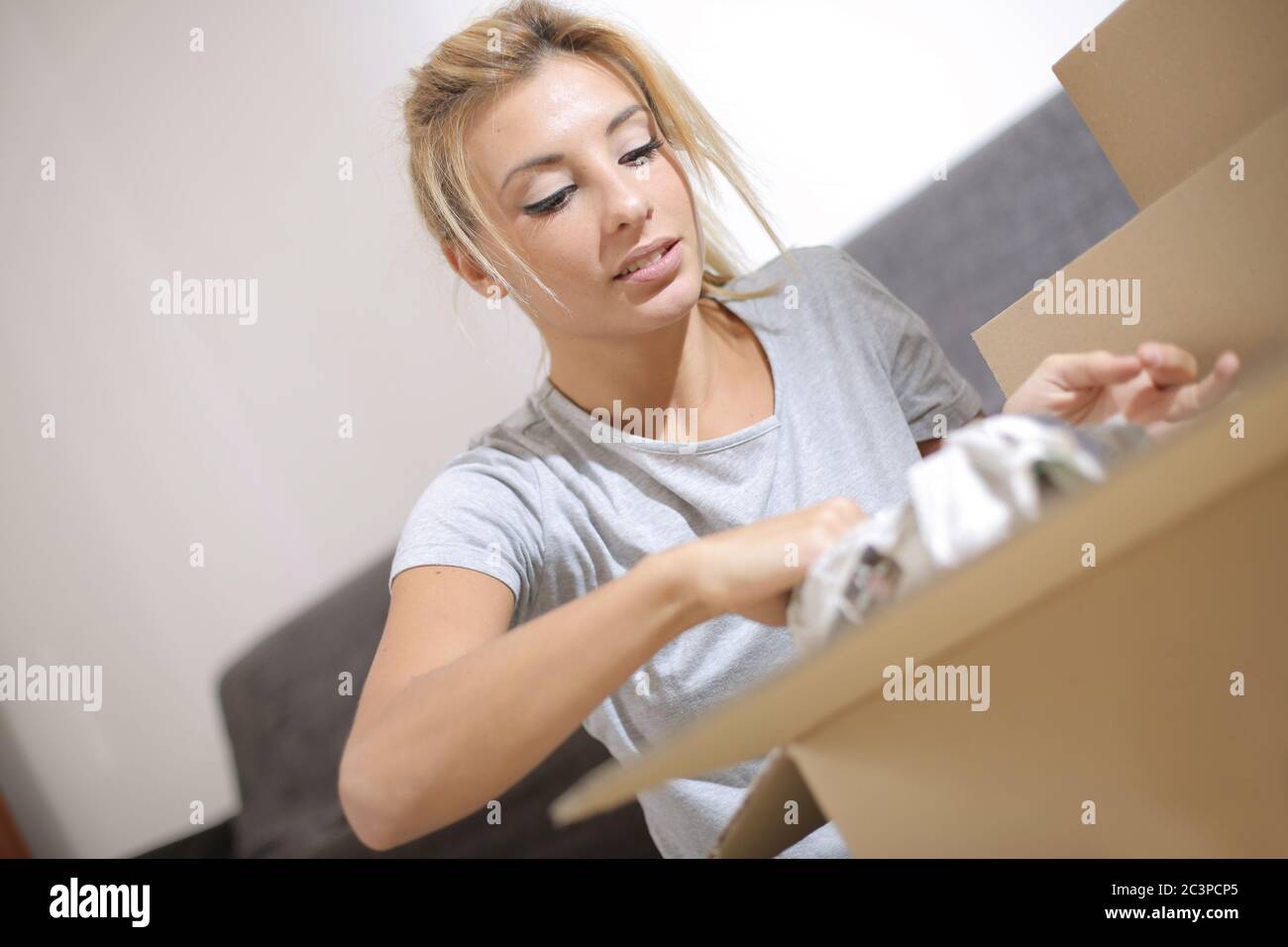 Young blonde female unpacking the boxes on the floor under the lights ...