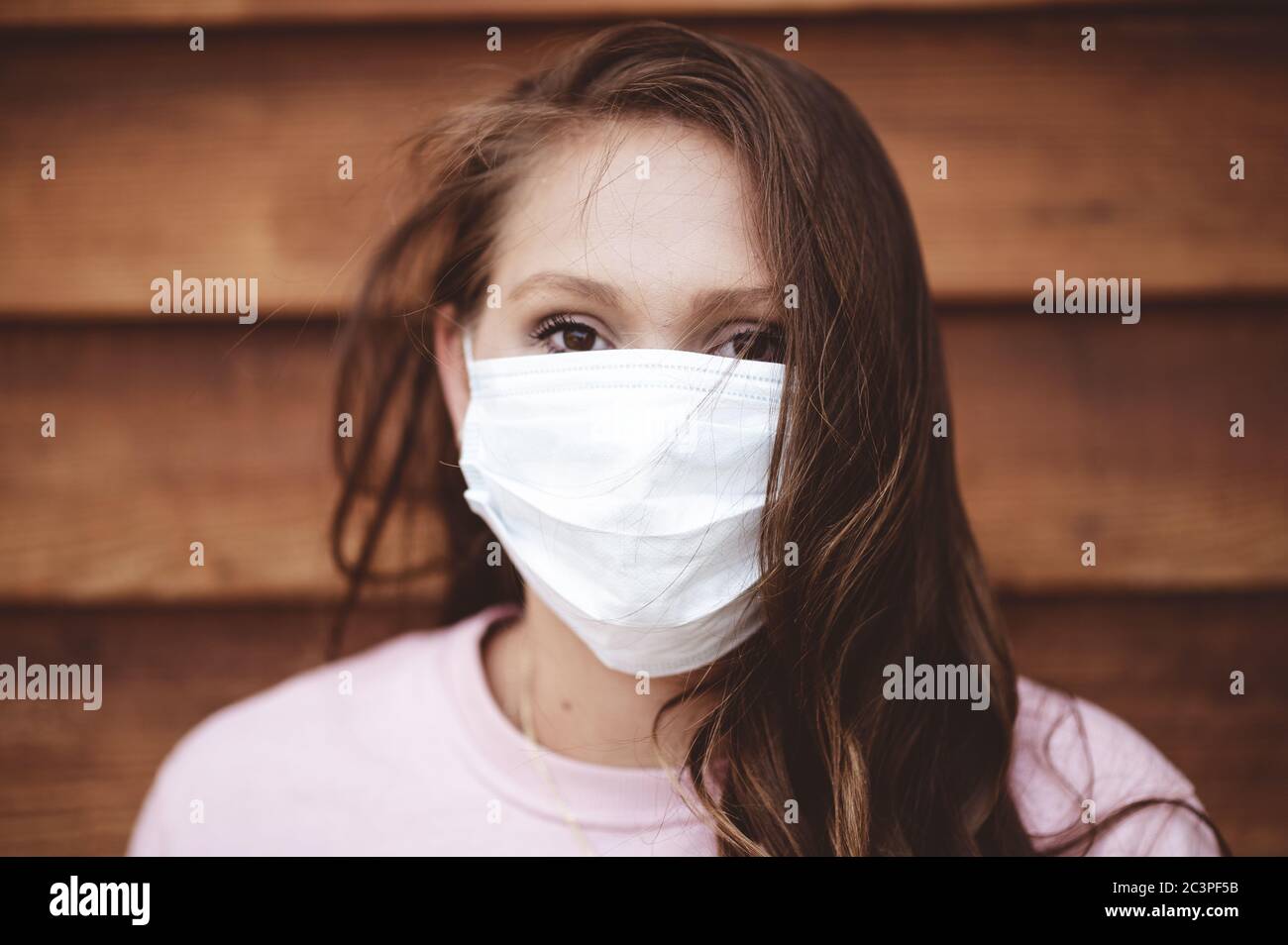Female wearing a sanitary face mask in front of a wooden wall ...