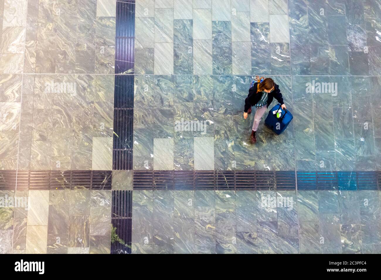 High angle shot of a female dragging a suitcase on the stone floor ...