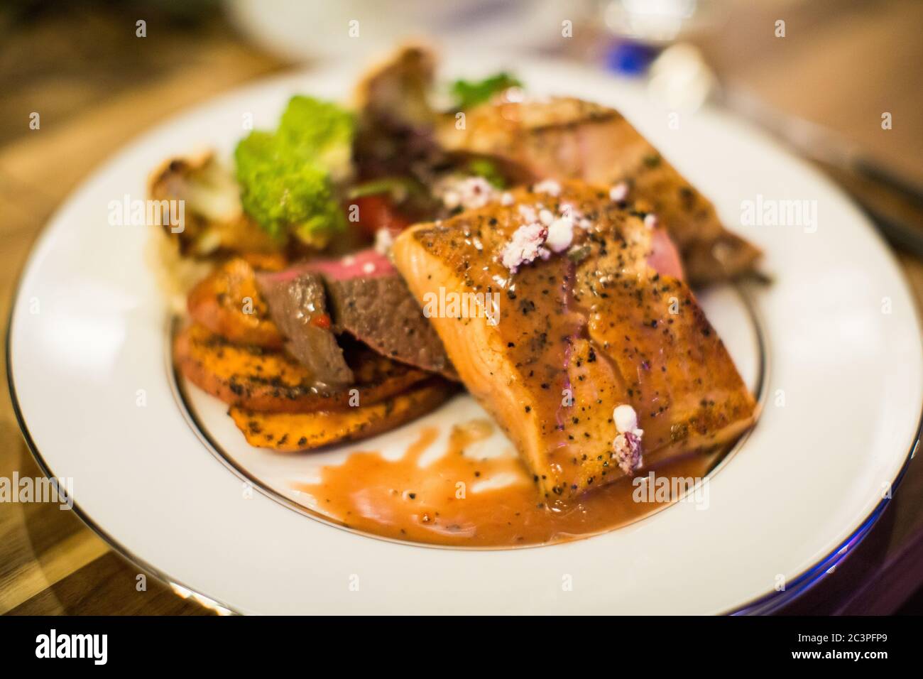 Closeup shot of cooked fish and beef with cauliflower and sauce in a ...