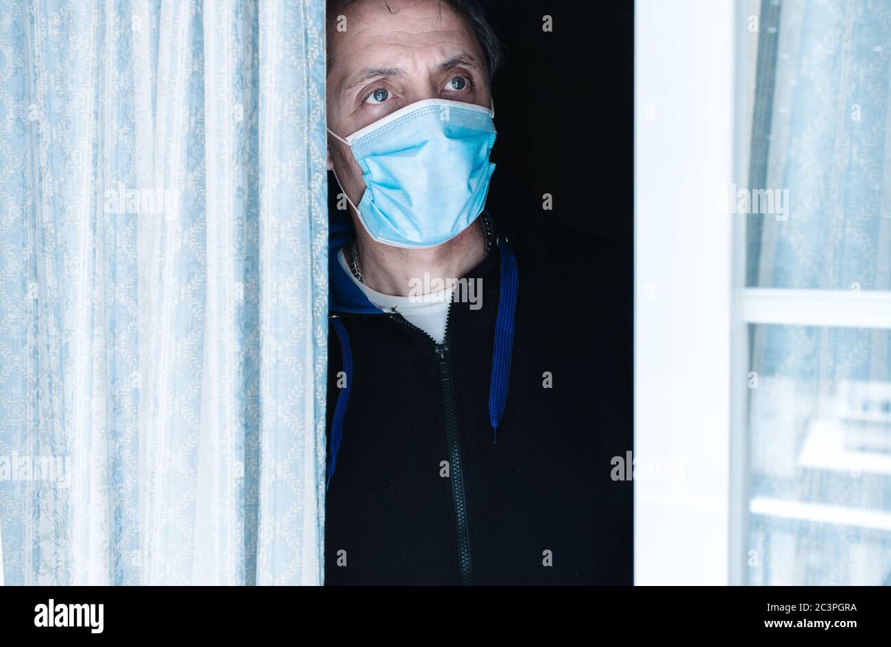Male wearing a sanitary face mask while standing behind a window ...