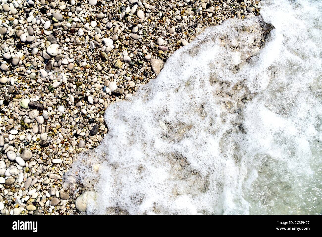 Colorful pebbles on the beach partly covered with foamed water ...