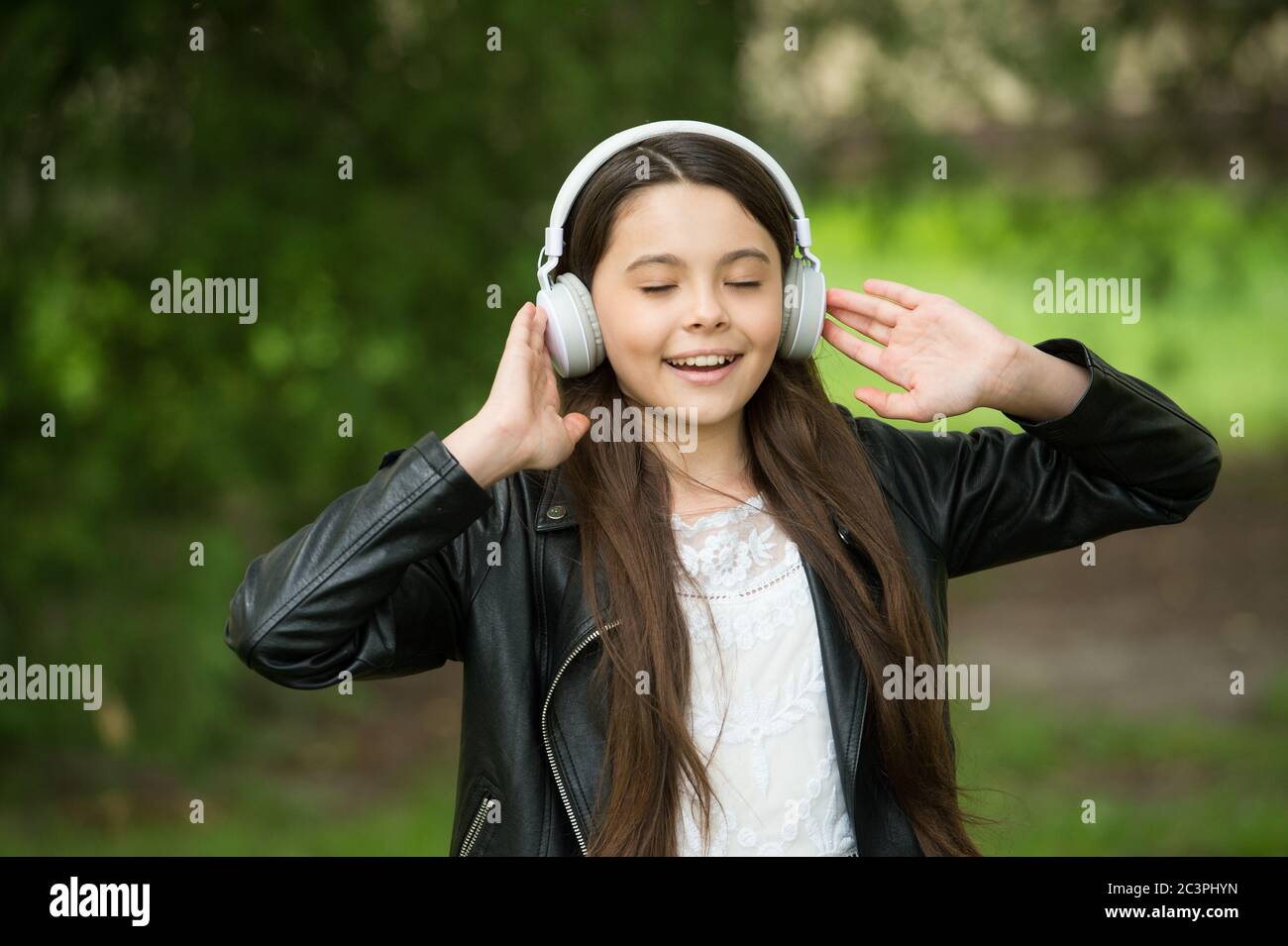 Shes ear for music. Happy child wear ear phones outdoors. Small girl ...