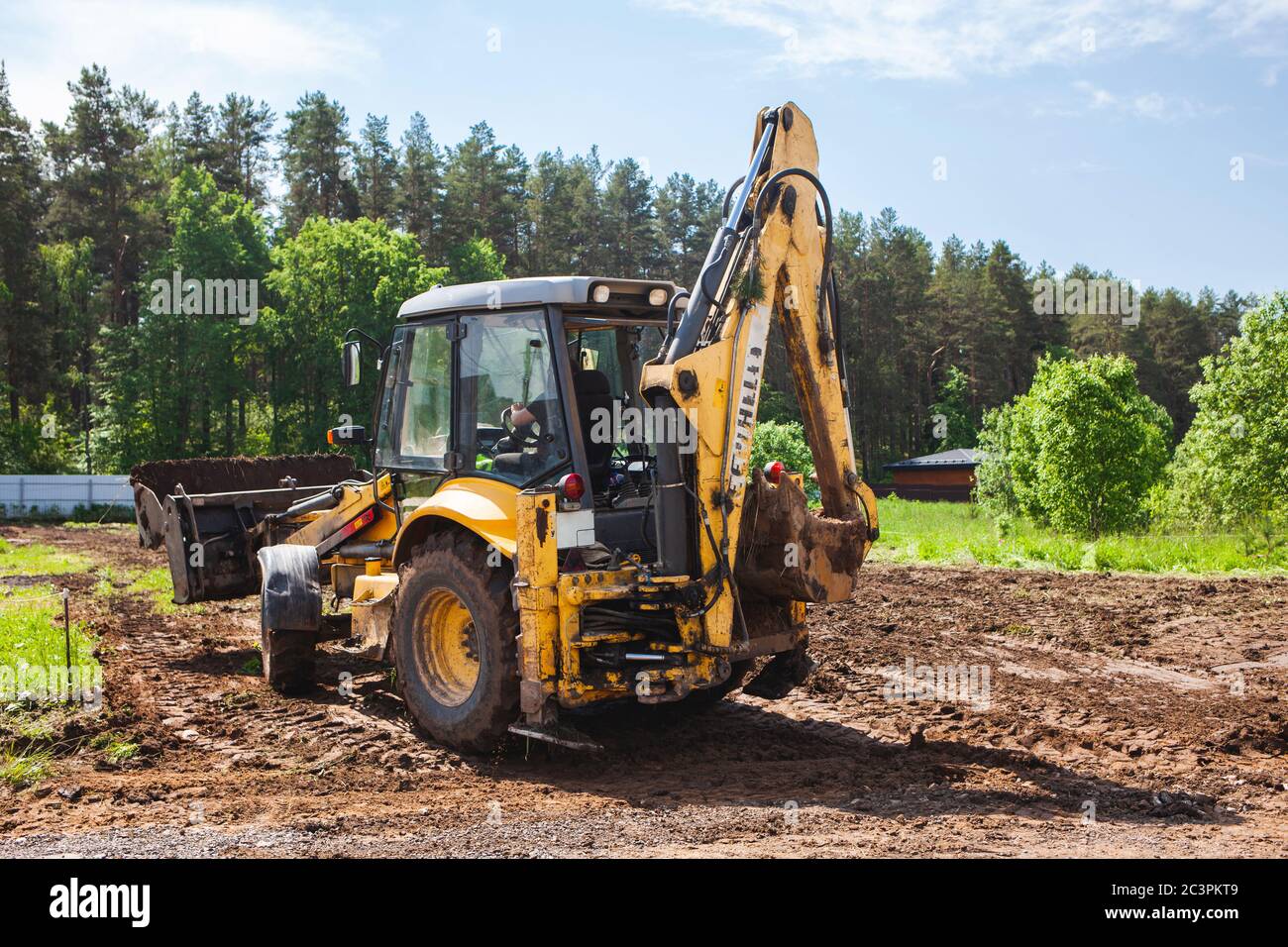 Clearing and leveling a private land plot. Yellow excavator driven ...