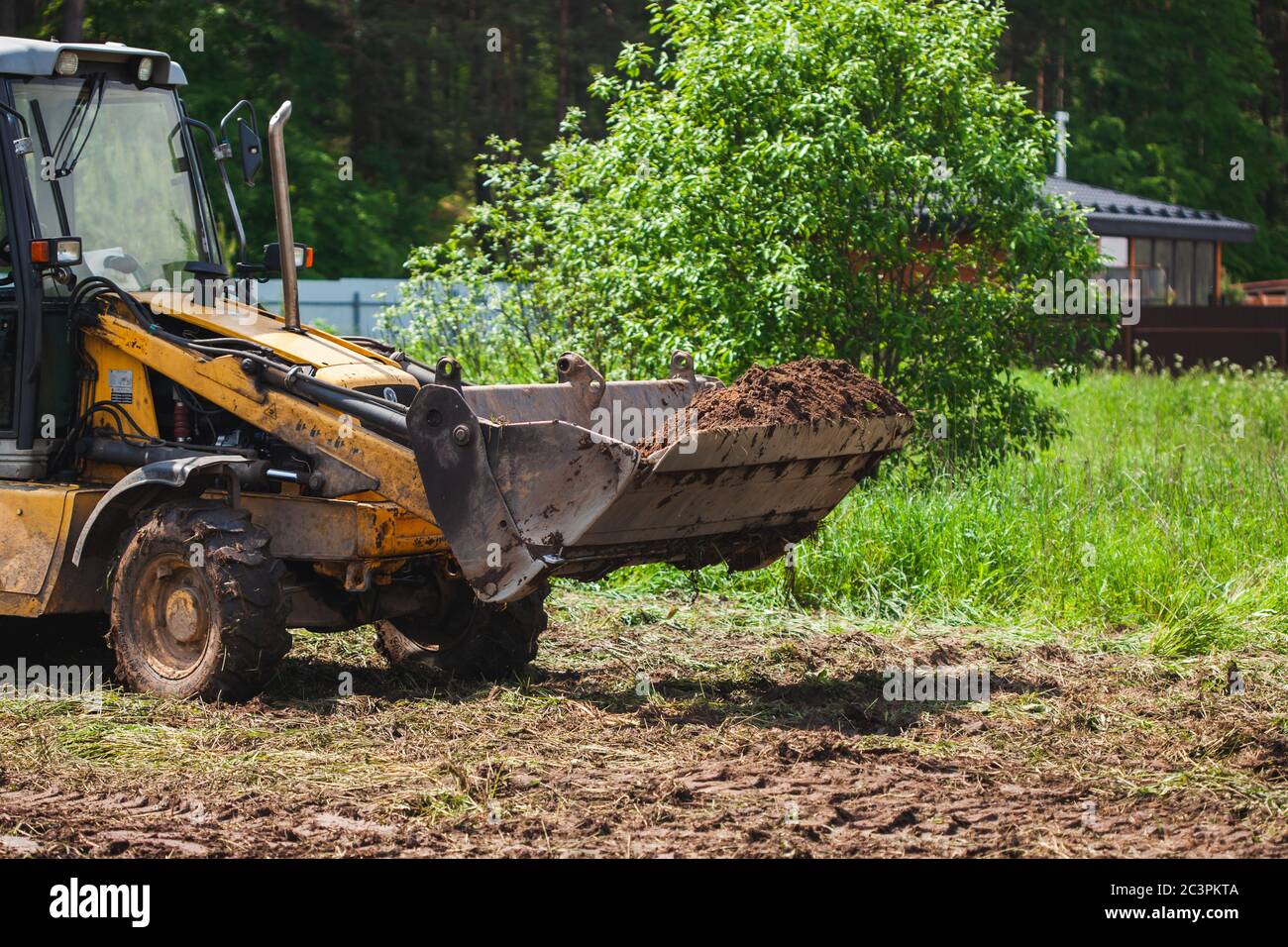 Clearing and leveling a private land plot. Yellow excavator driven ...