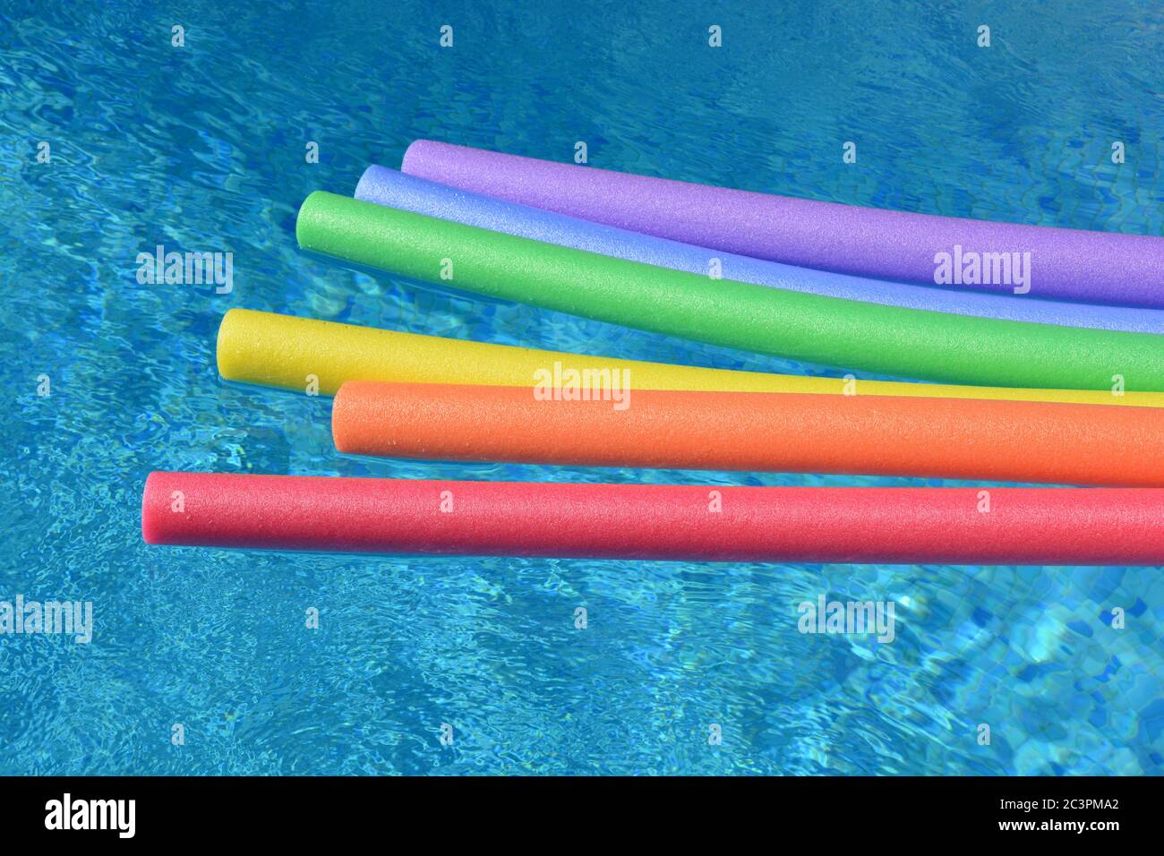 Rainbow coloured pool noodles floating in a swimming pool on a bright ...