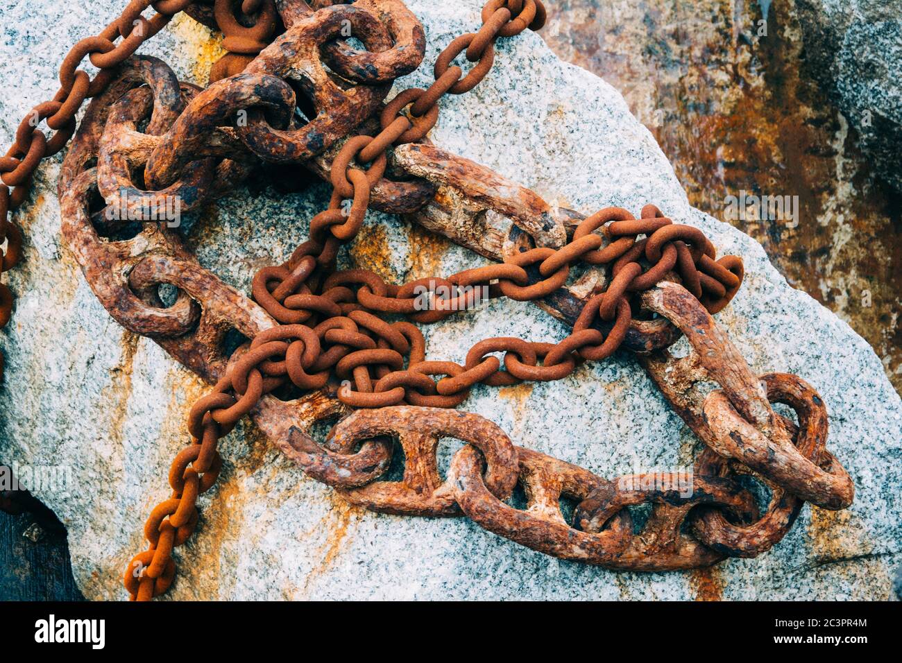 Horizontal shot of many rusted chains of different sizes on a big stone ...