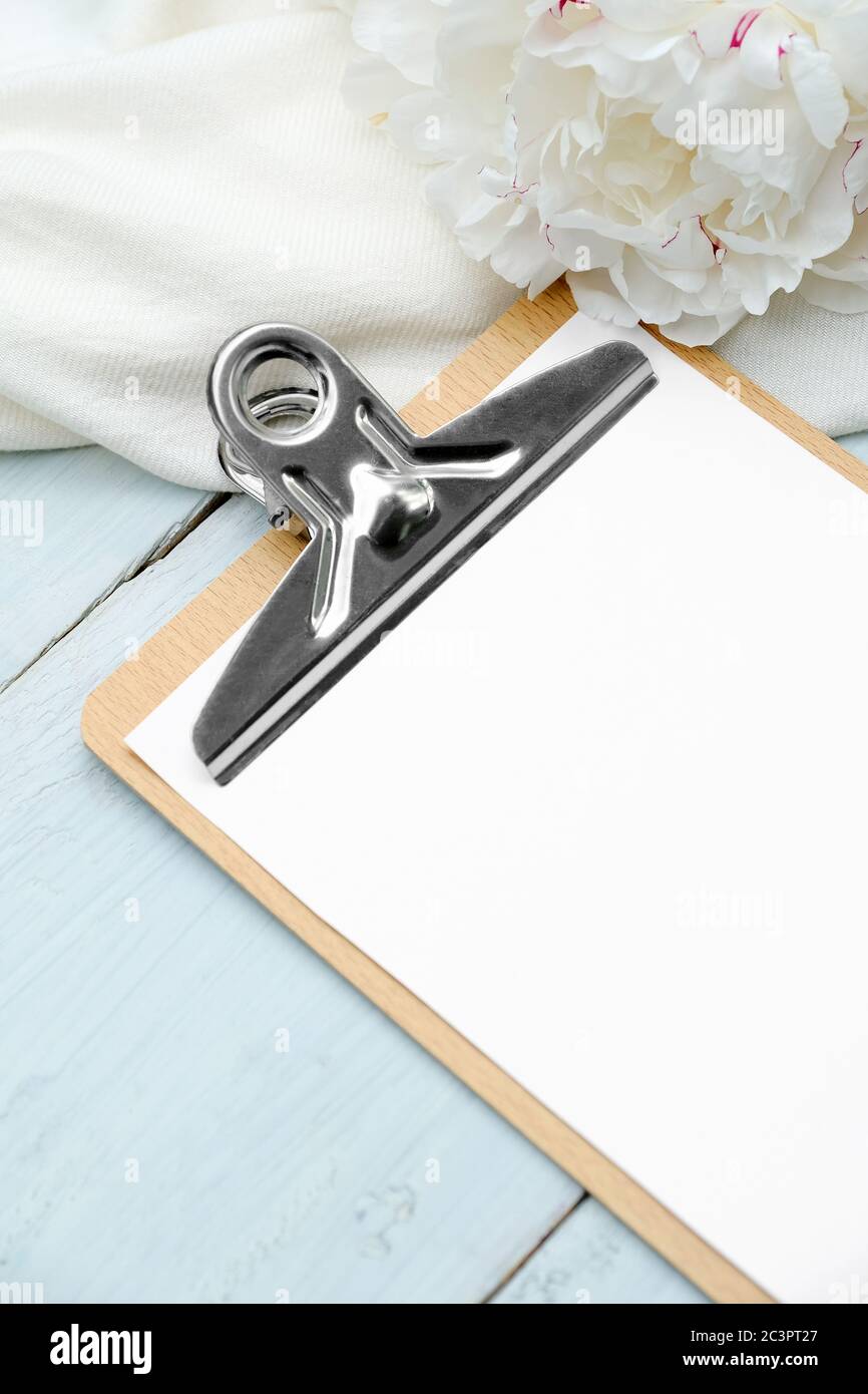 Clipboard with blank paper mockup and peonies on wooden table, top view ...