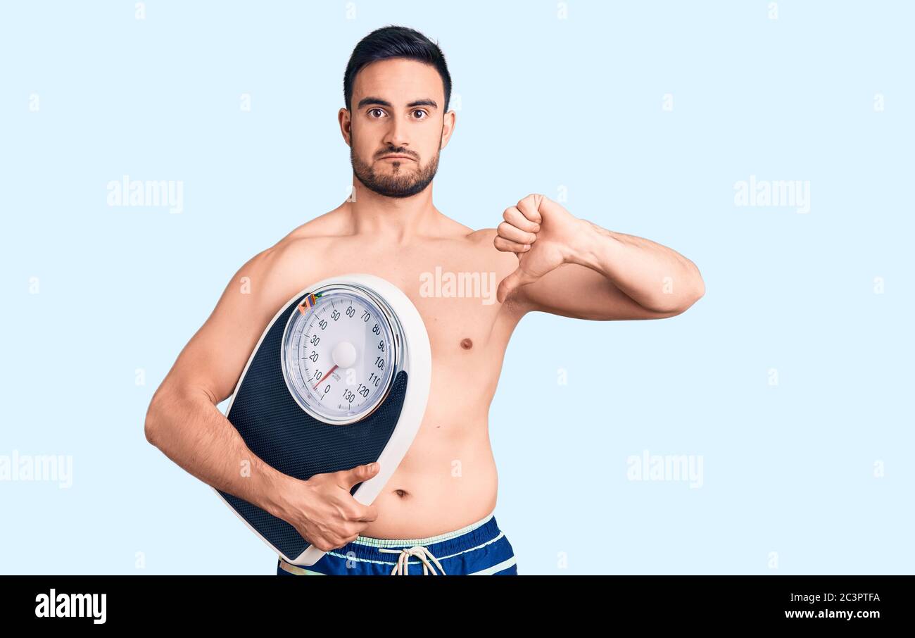 Young handsome man wearing swimwear holding weighing machine with angry ...