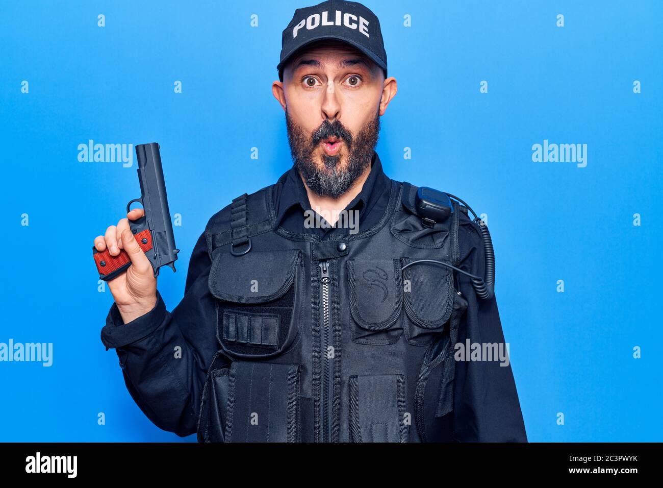 Young handsome man wearing police uniform holding gun scared and amazed ...
