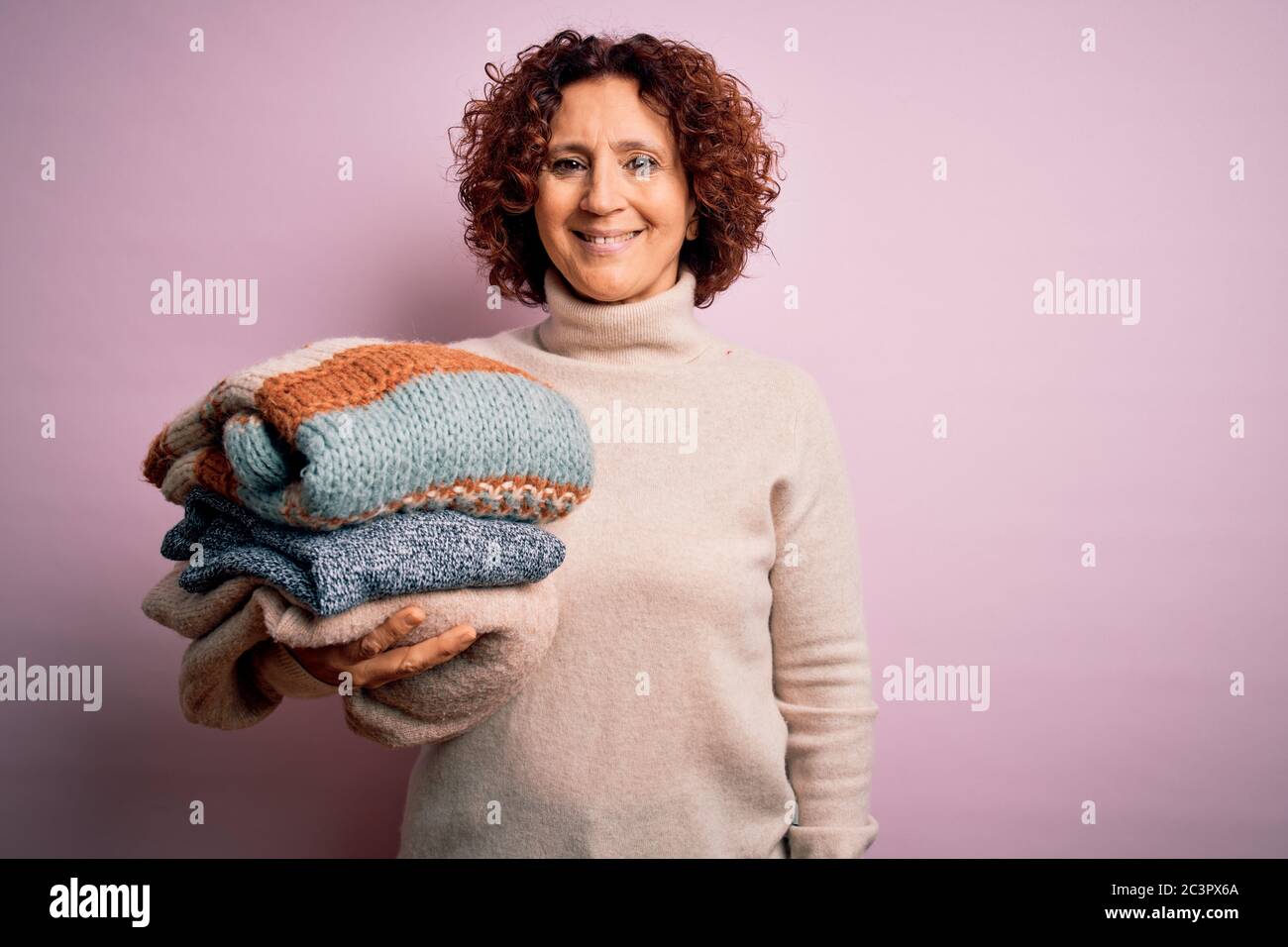 Middle age curly hair housework woman holding pile of clothes over ...