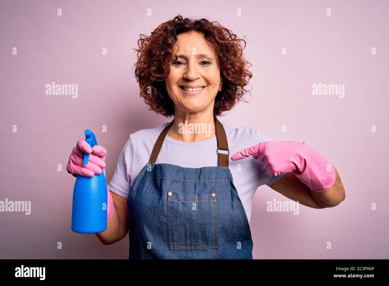 Middle age curly hair woman cleaning doing housework wearing apron and ...