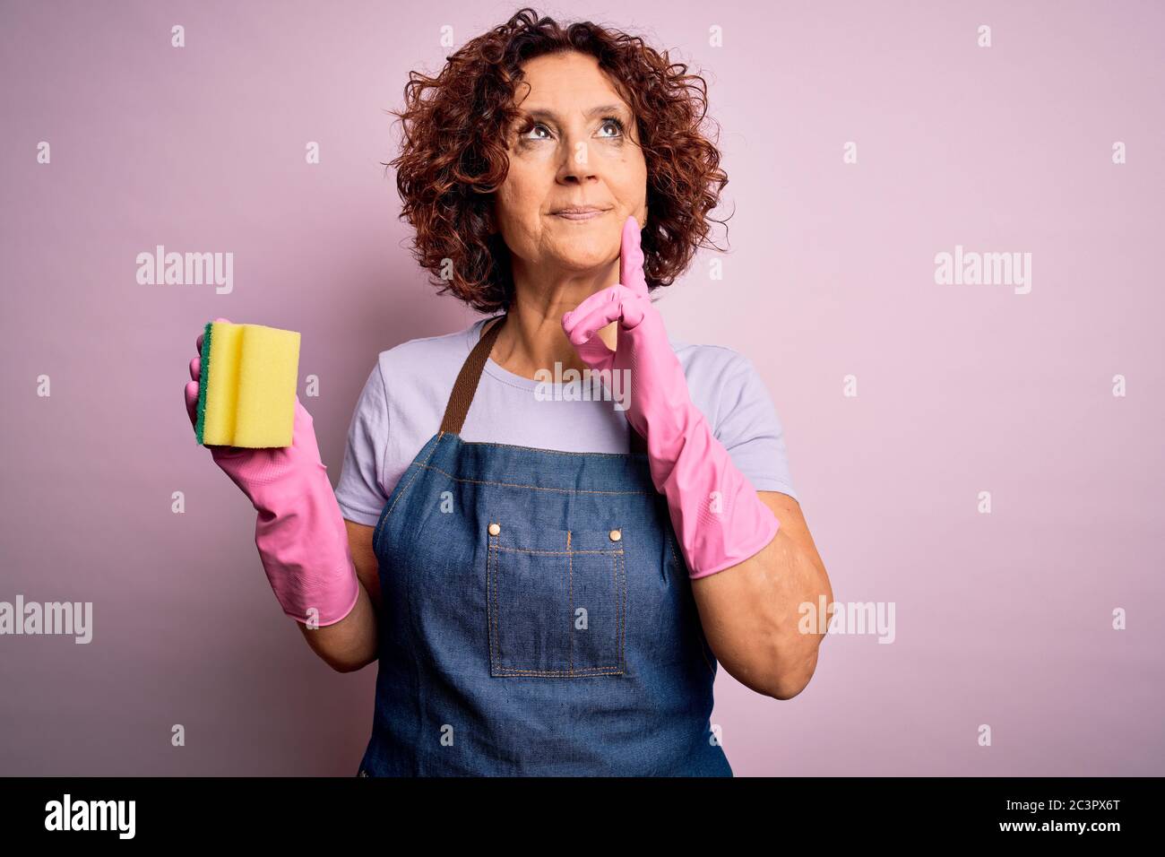 Middle age curly hair woman cleaning doing housework wearing apron and ...