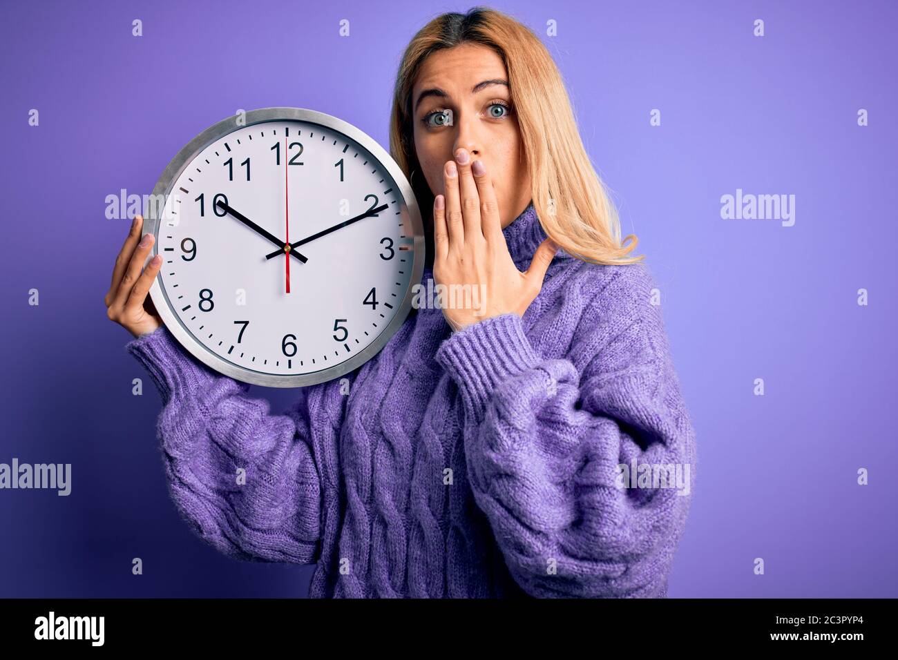 Young beautiful blonde woman doing countdown holding big clock over ...