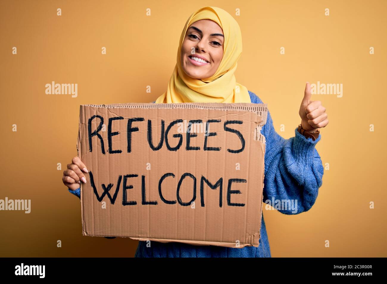 Beautiful arab woman wearing islamic hijab holding banner with refugees ...