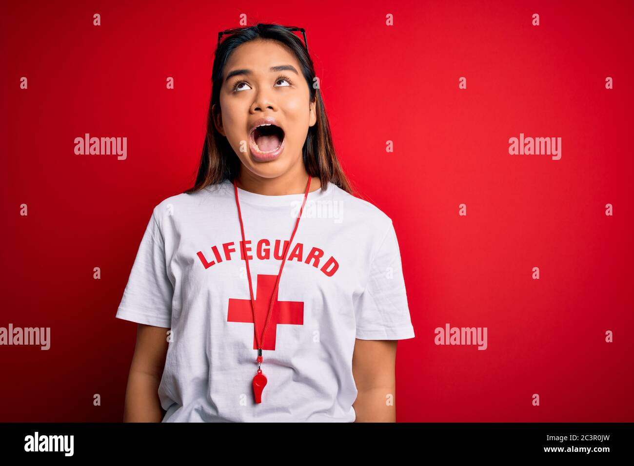 Young asian lifeguard girl wearing t-shirt with red cross using whistle ...