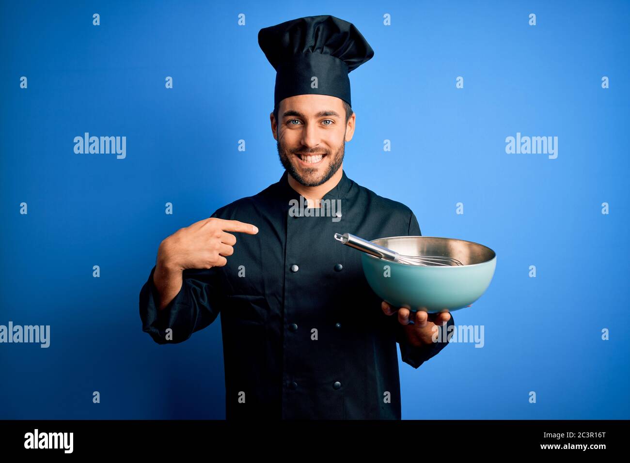 Young cooker man with beard wearing uniform using whisk and bowl over ...