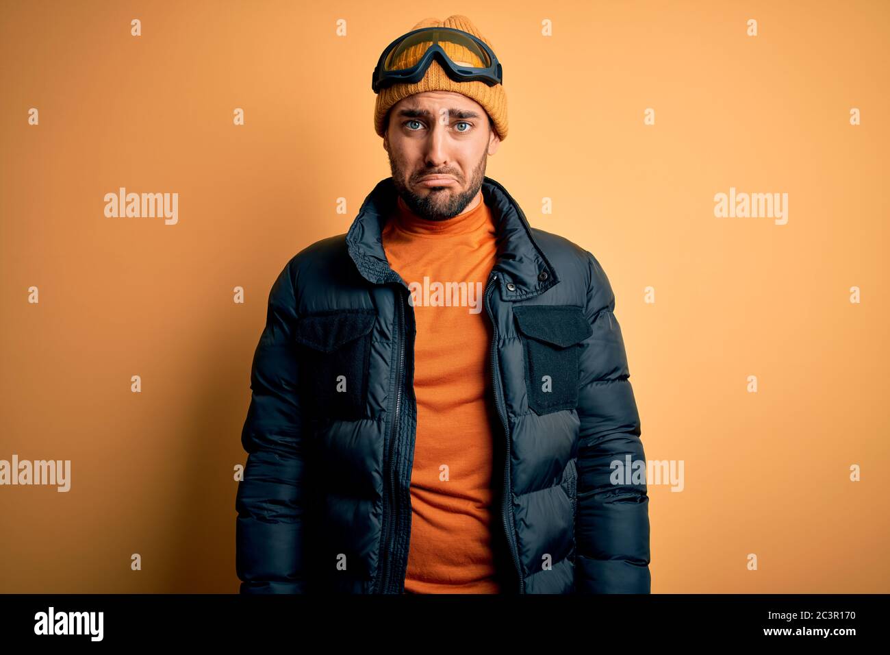 Young handsome skier man with beard wearing snow sportswear and ski ...