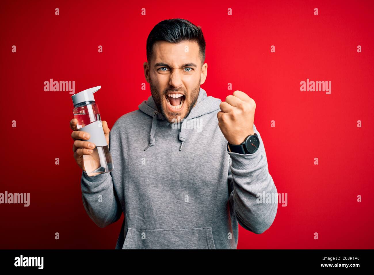 Young handsome sportsman drinking bottle of water to refeshment over ...