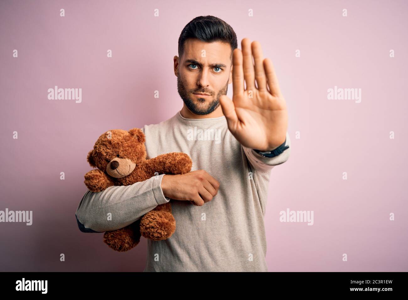 Young handsome man holding teddy bear standing over isolated pink ...