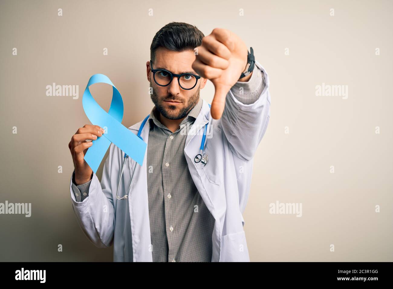 Young professional doctor man holding colon awareness blue ribbon over ...