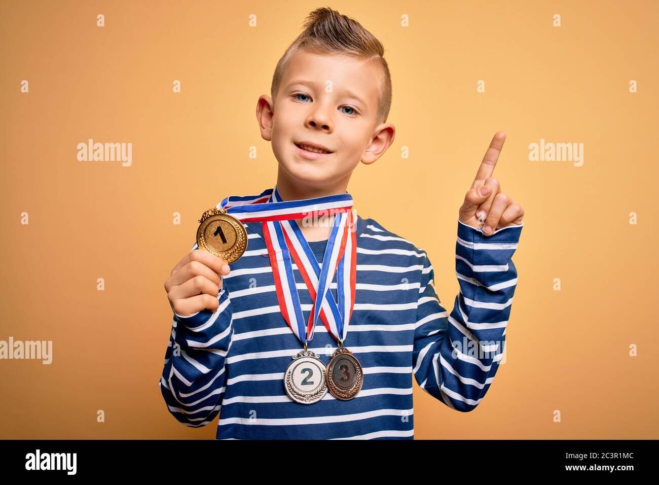 Young little caucasian winner kid wearing award competition medals over ...
