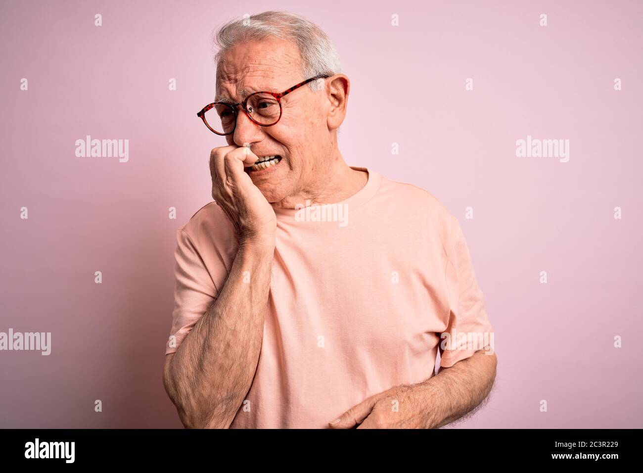 Grey haired senior man wearing glasses standing over pink isolated ...