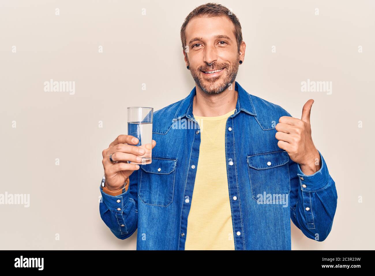 Young handsome man drinking glass of water smiling happy and positive ...