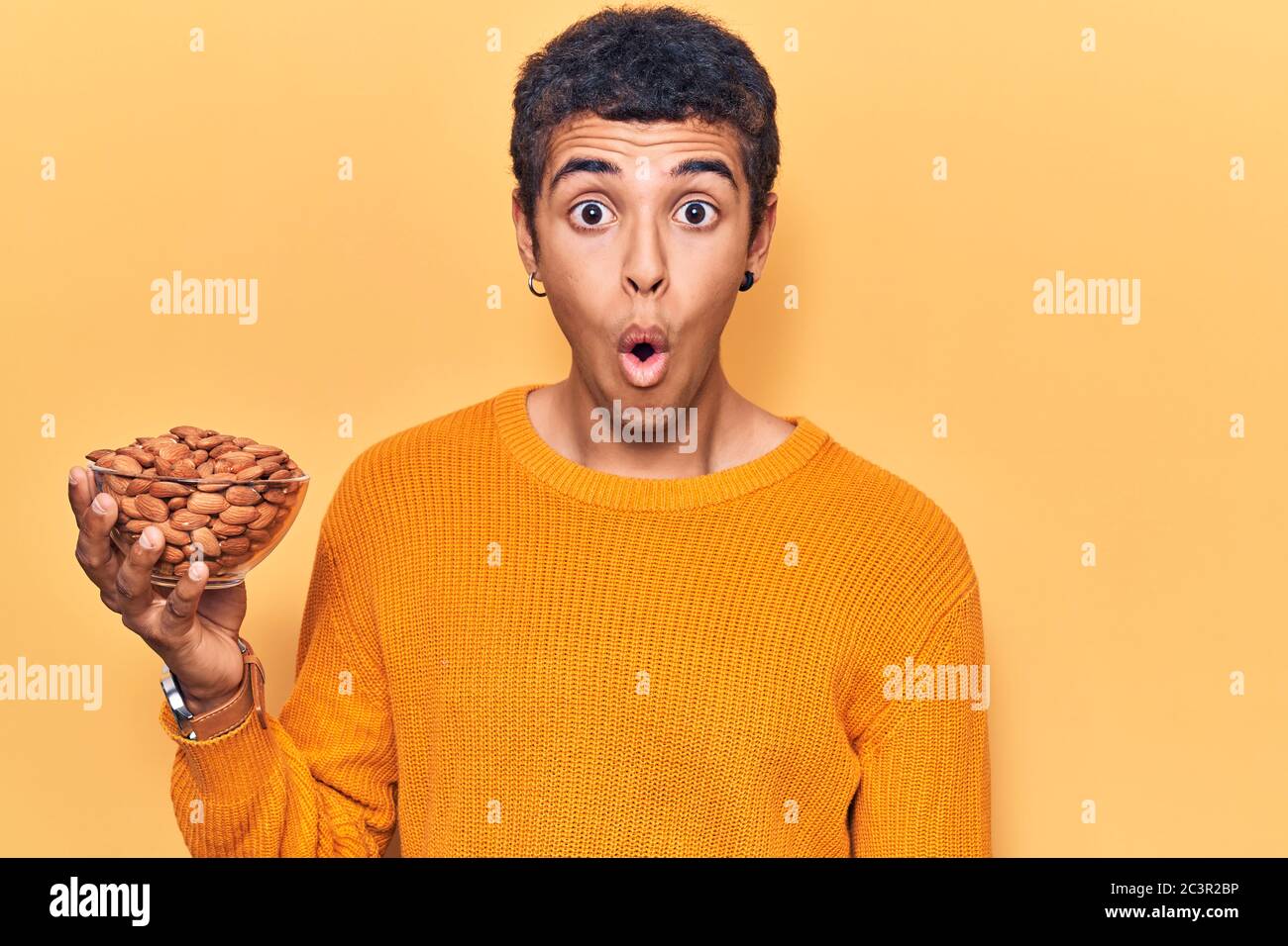 Young african amercian man holding bowl with almonds scared and amazed ...
