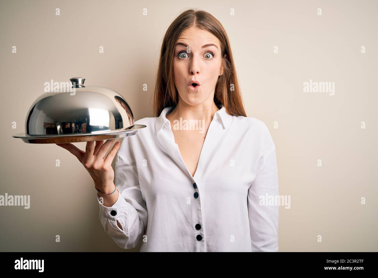 Young beautiful redhead woman holding waitress tray over isolated white ...
