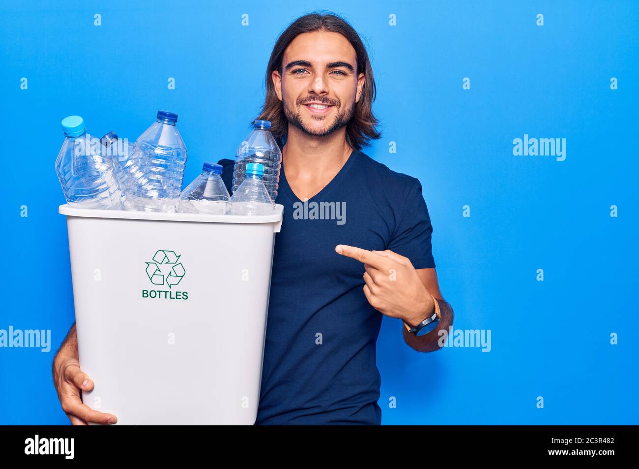 Young handsome man holding recycling wastebasket with plastic bottles ...