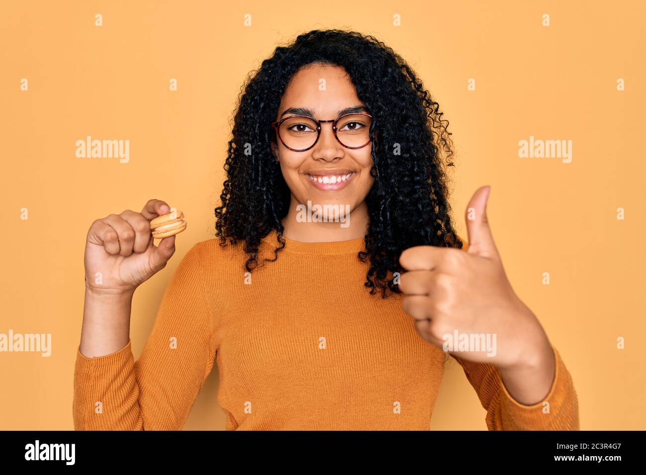 Young african american curly woman wearing glasses eating delicious ...