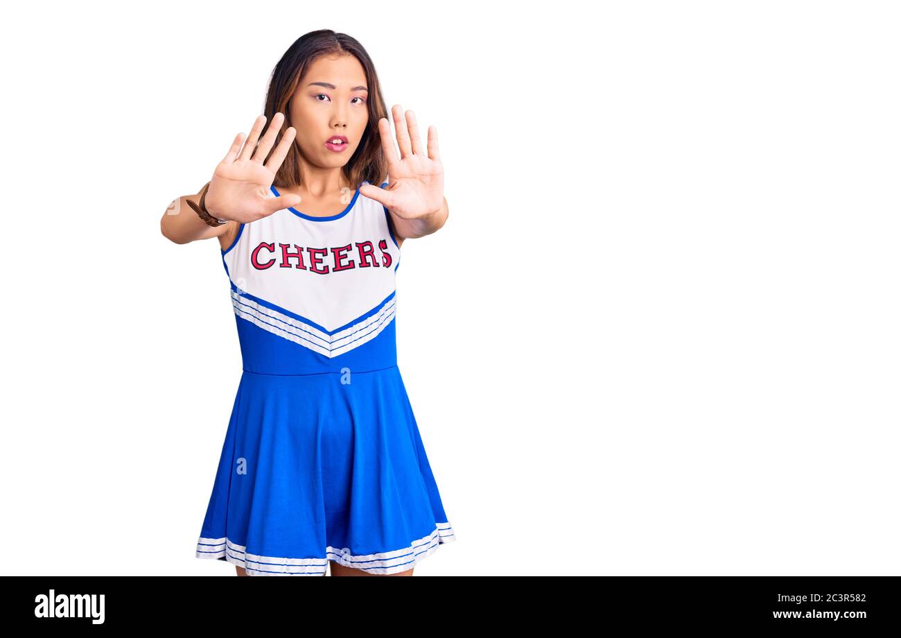 Young beautiful chinese girl wearing cheerleader uniform doing stop ...