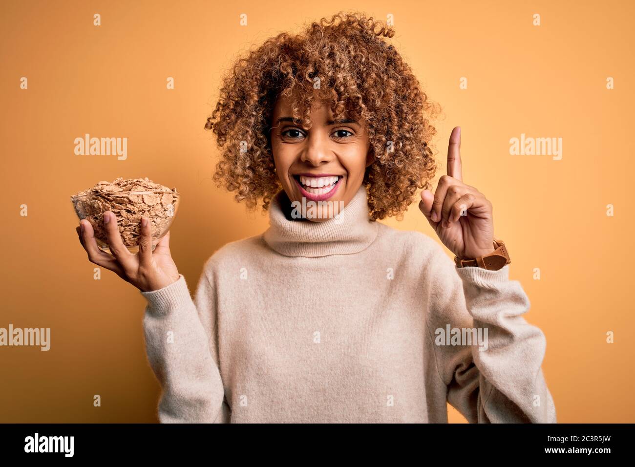 Young african american curly woman holding bowl with healthy cornflakes ...