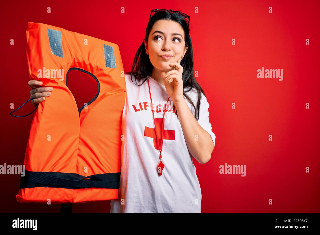 Young lifeguard woman holding rescue lifejacket over red background ...