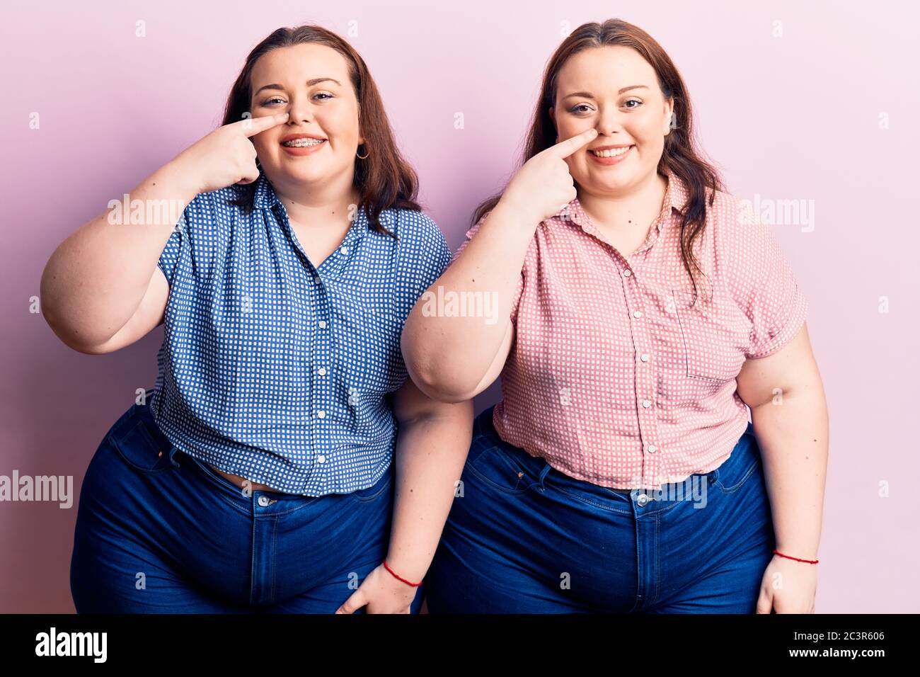 Young plus size twins wearing casual clothes pointing with hand finger ...