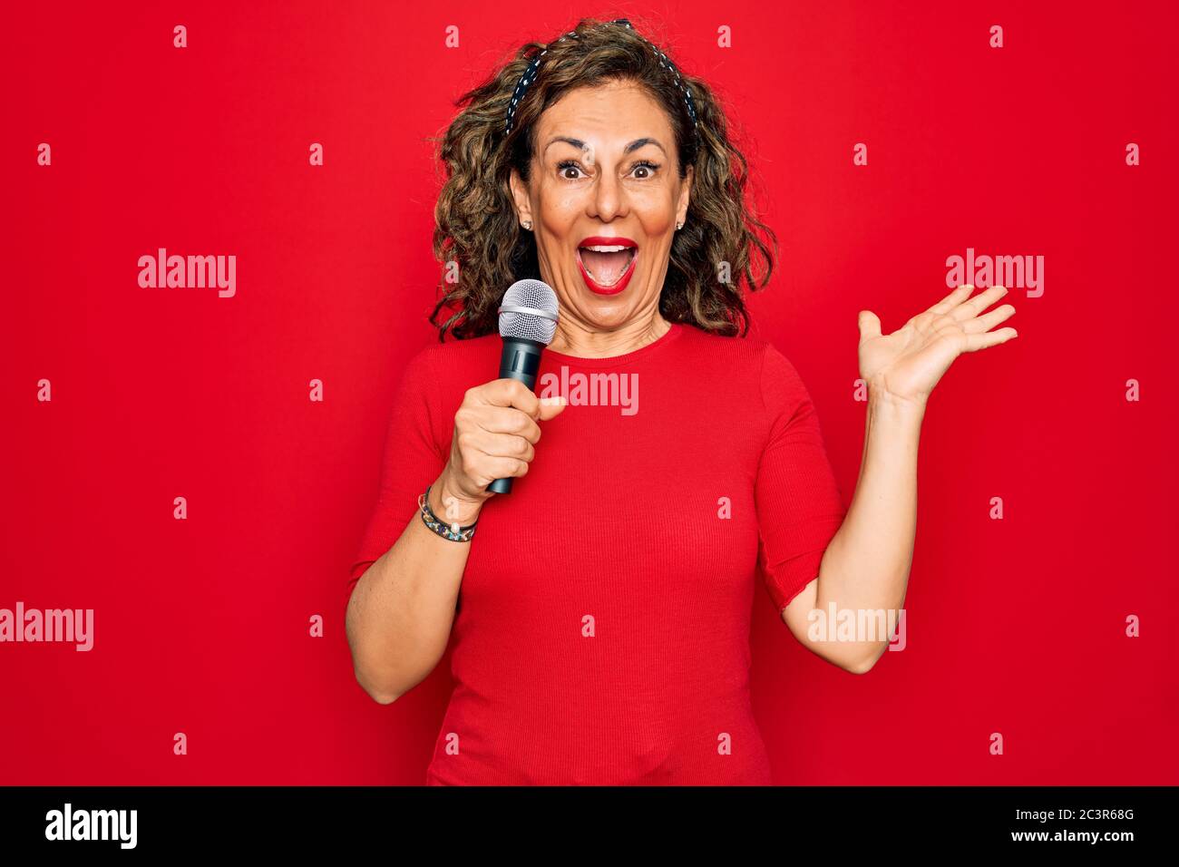 Middle age senior singer woman singing using music microphone over red ...