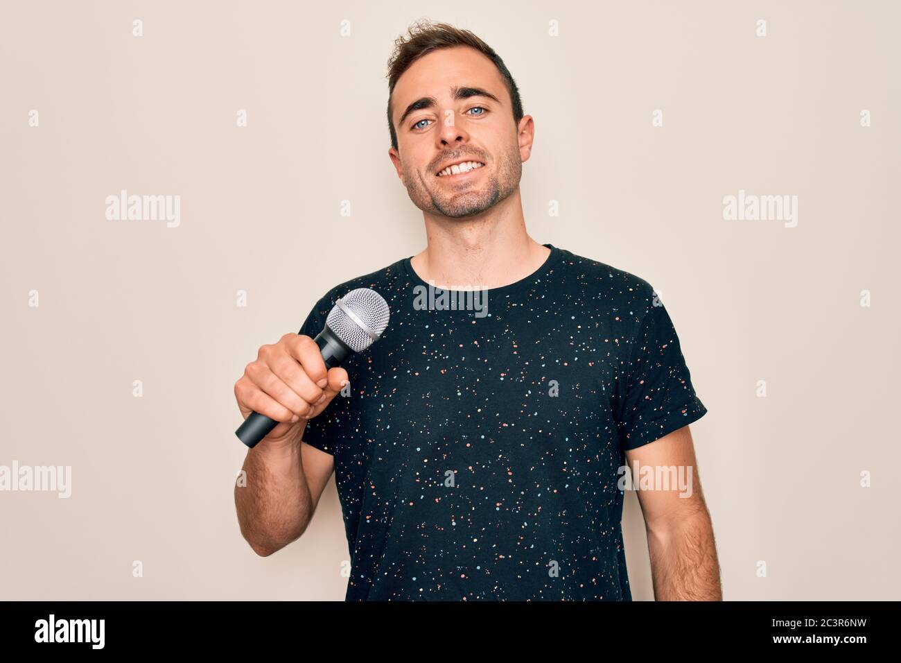 Young handsome singer man with blue eyes singing using microphone over white background with a ...