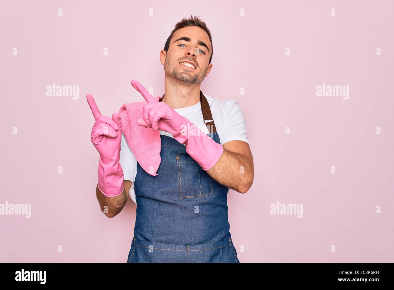 Young cleaner man with blue eyes cleaning wearing apron and gloves over ...